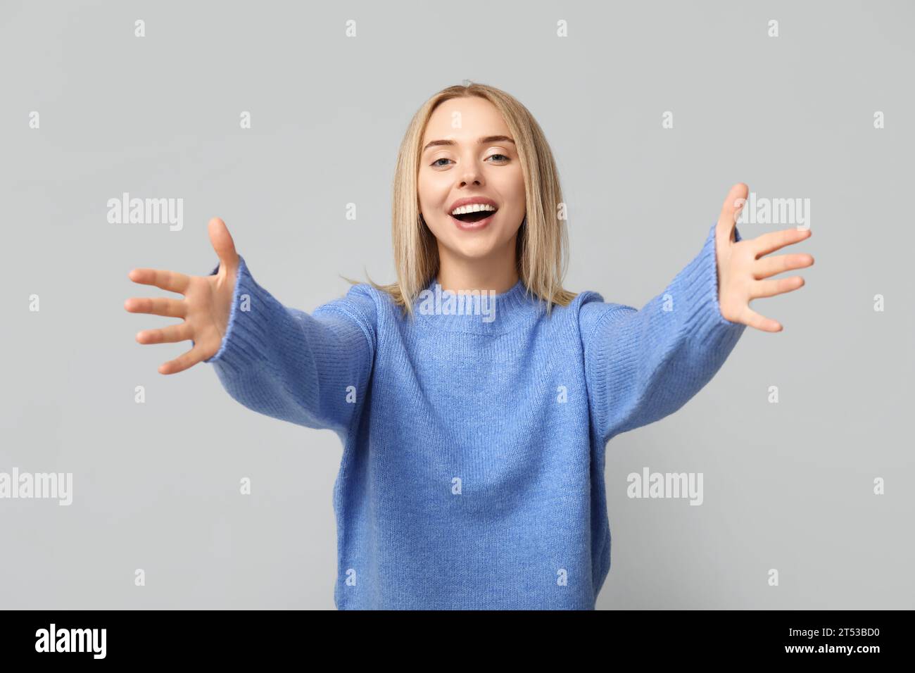 Young woman opening arms for hug on grey background Stock Photo - Alamy