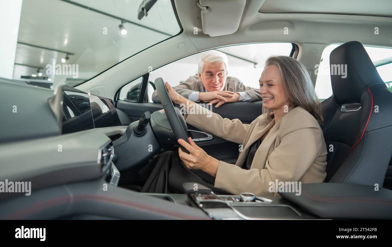 An elderly couple chooses a new car at a car dealership. Mature woman ...