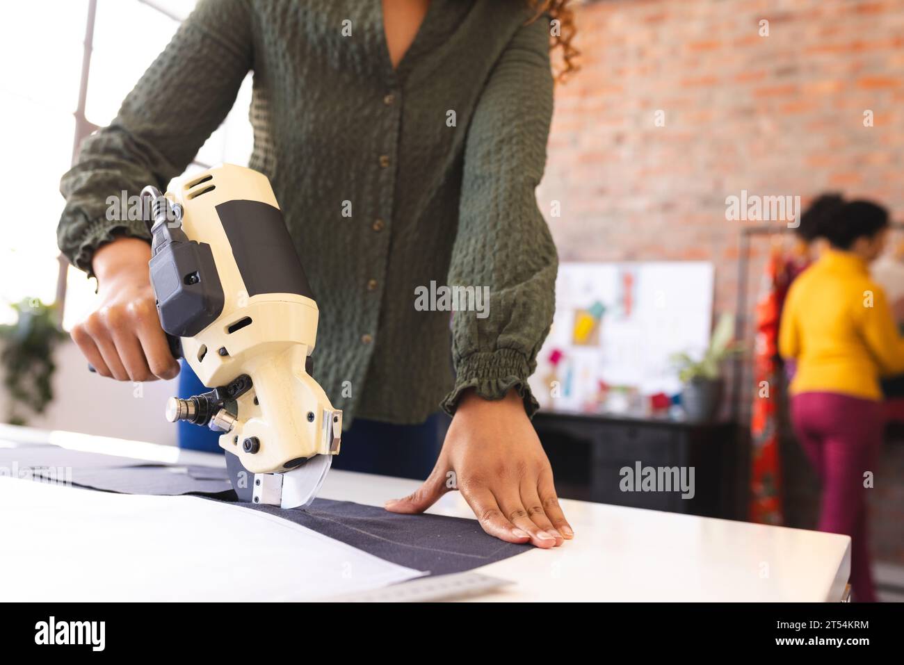 Biracial female fashion designer using rotary fabric cutter in sunny ...