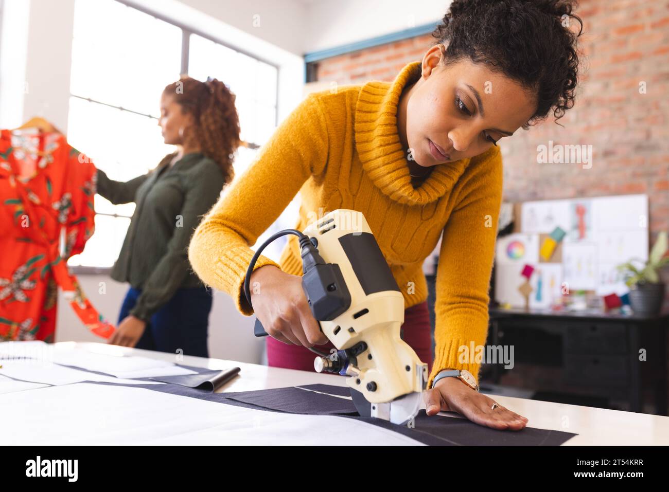 Focused biracial female fashion designer using rotary fabric cutter in ...