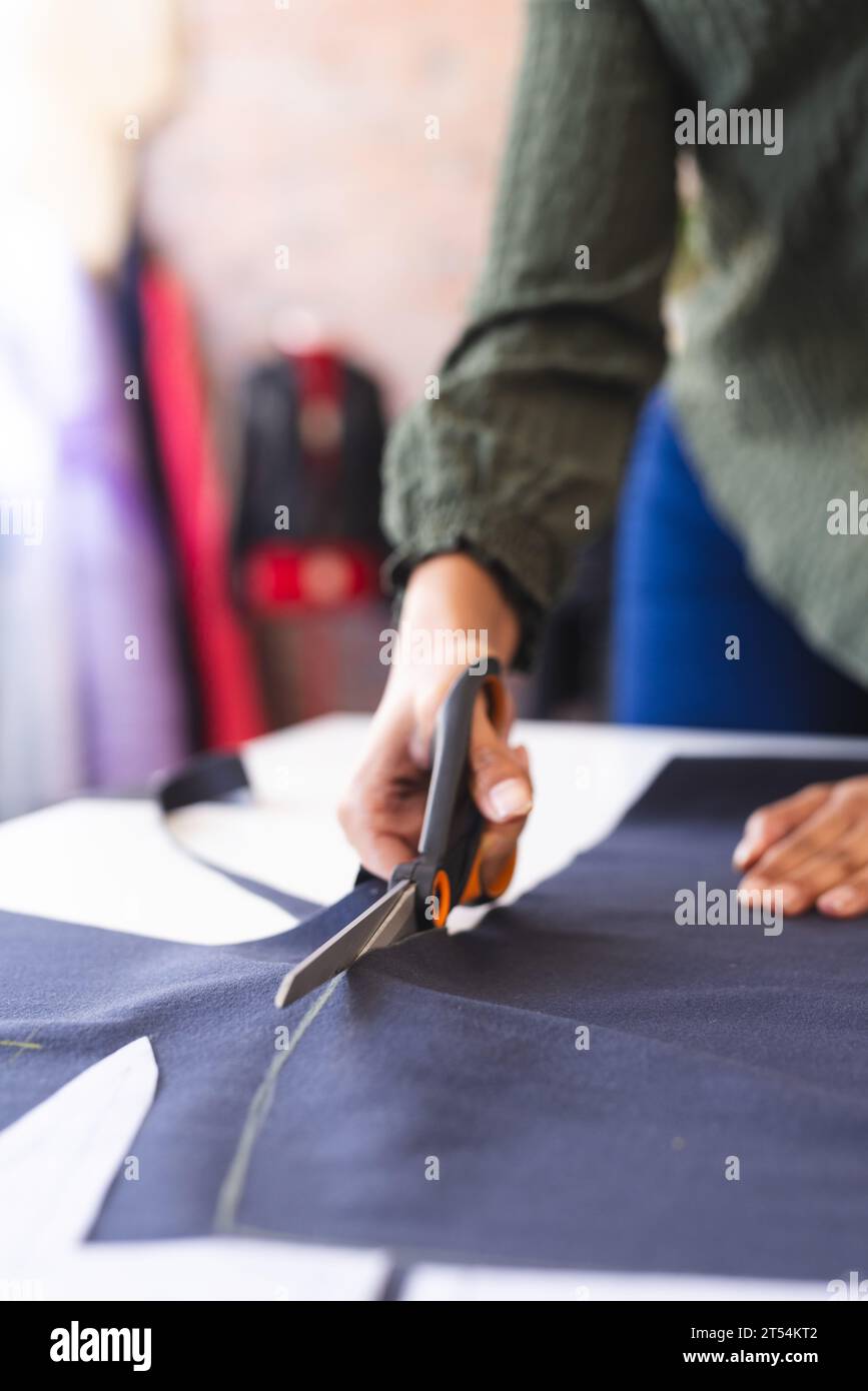 Biracial female fashion designer cutting fabric with scissors in sunny ...