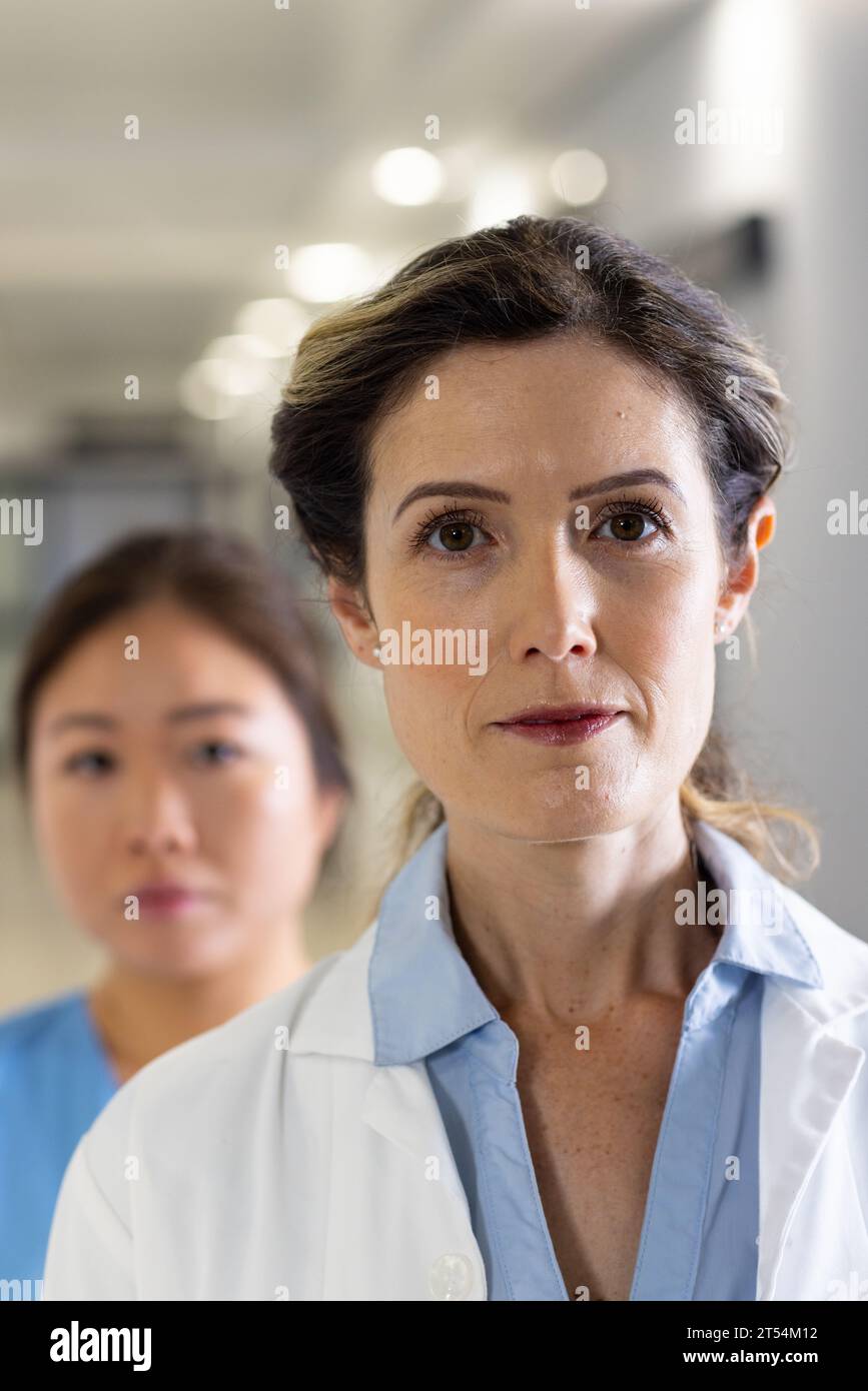 Two diverse female doctors standing single file in hospital corridor ...
