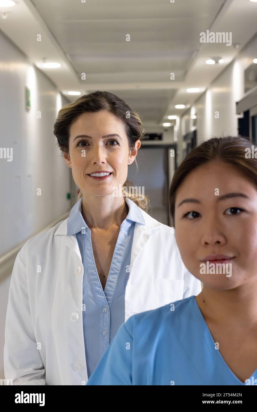Two happy diverse female doctors standing single file in hospital ...
