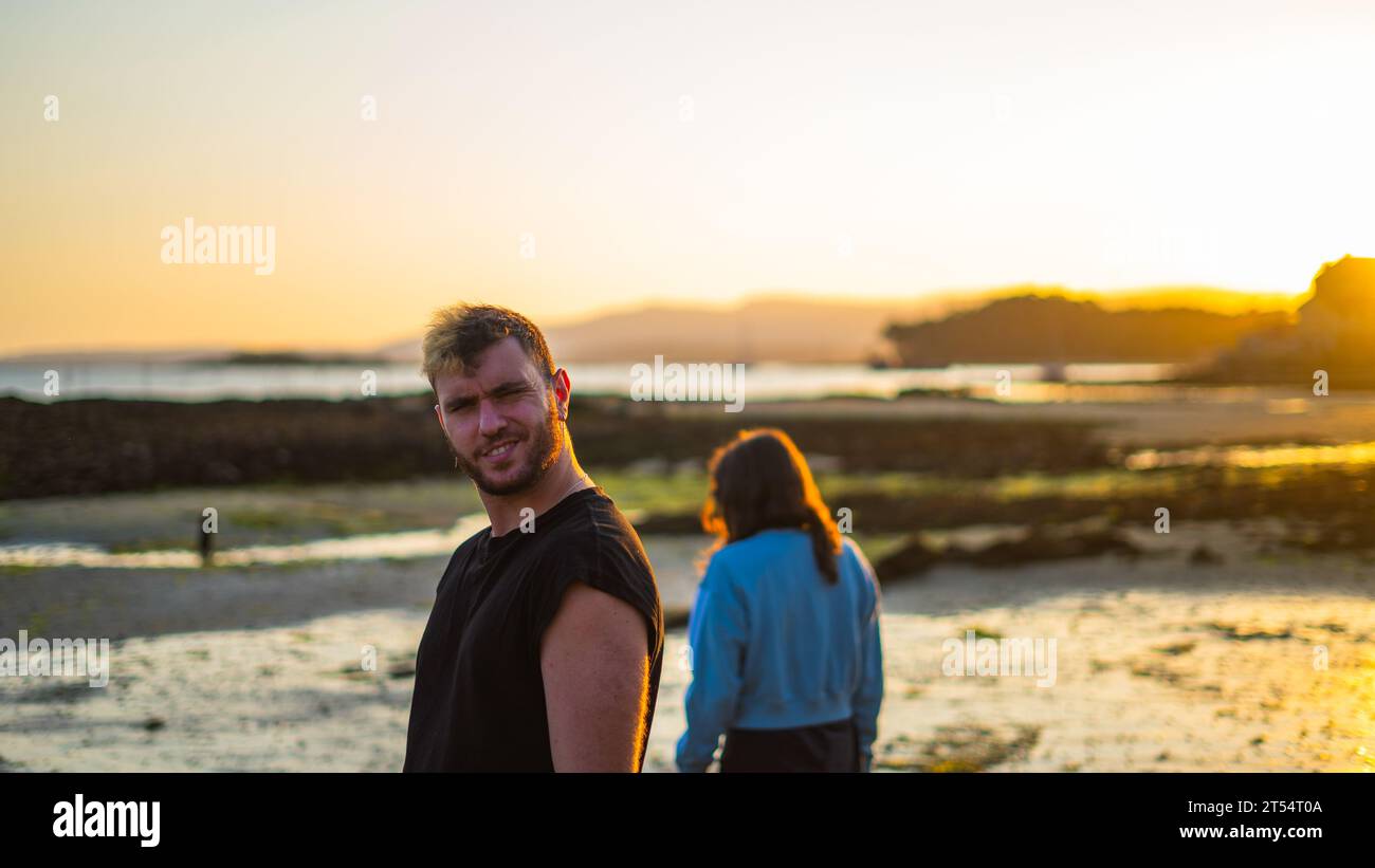 young atractive man winking looking at the camera with the beach in the ...