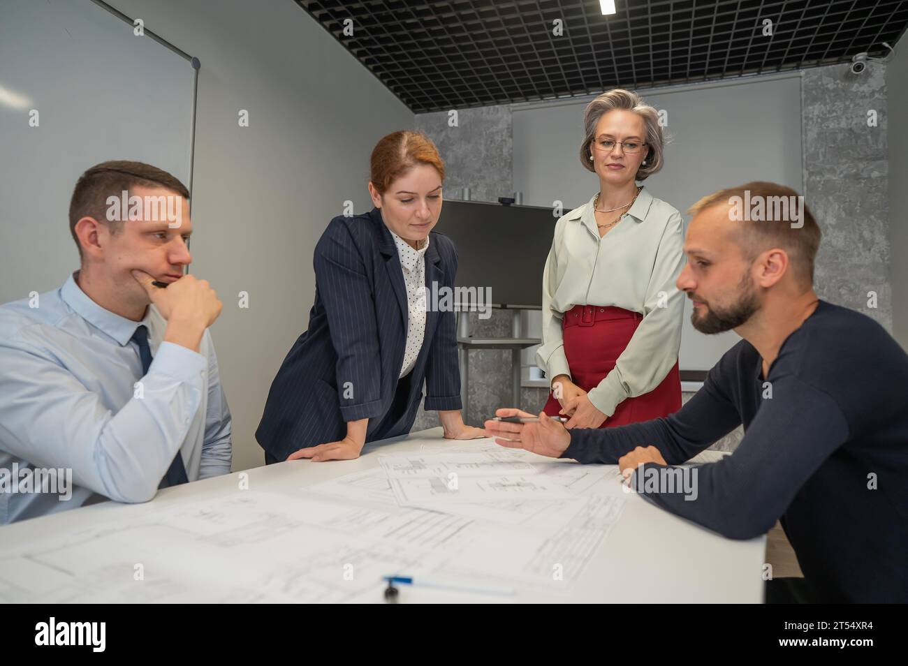 Four business people sitting around a table discussing blueprints ...
