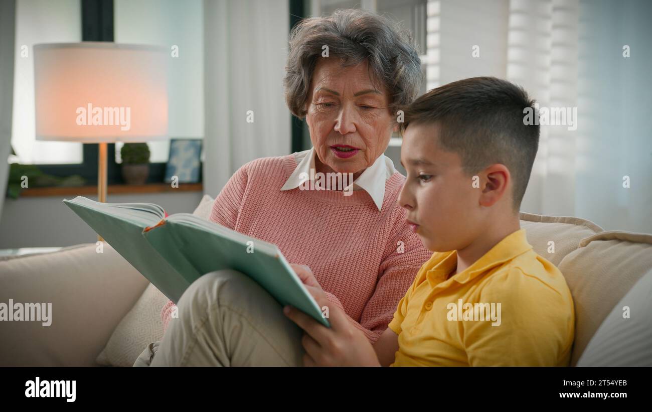 Loving elderly woman retired grandmother reading book with grandson at ...