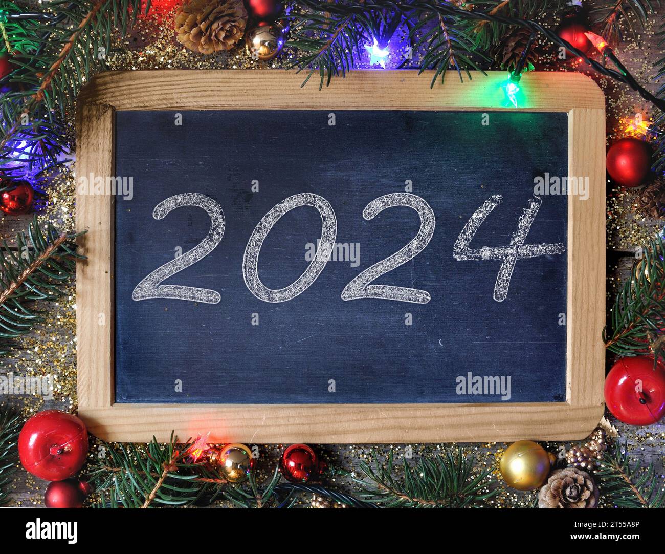 year 2024 written on a chalk slate surrounded by Christmas decorations ...