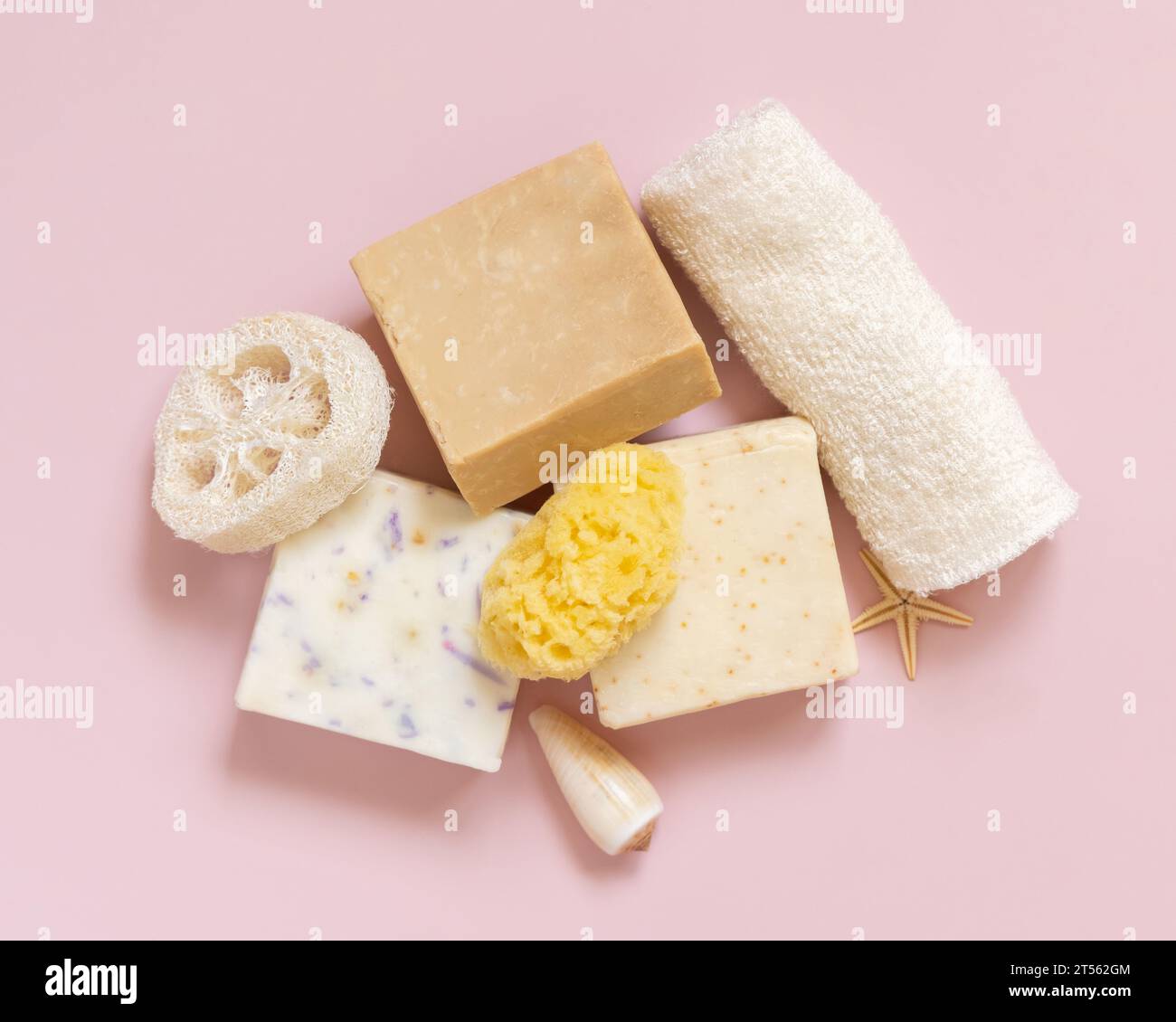 Beige soap bars, seashells, natural sponges and towel on light pink top ...