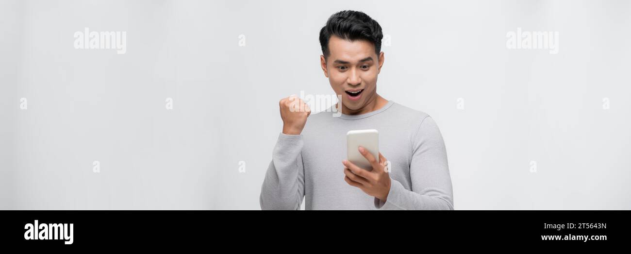 Excited asian man isolated on white background look at smartphone happy ...