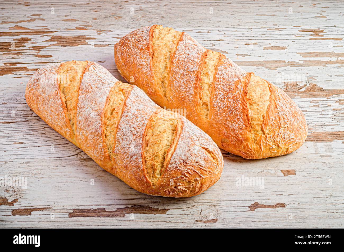 Two fresh, golden-brown loaves of bread side by side on a rustic wooden ...