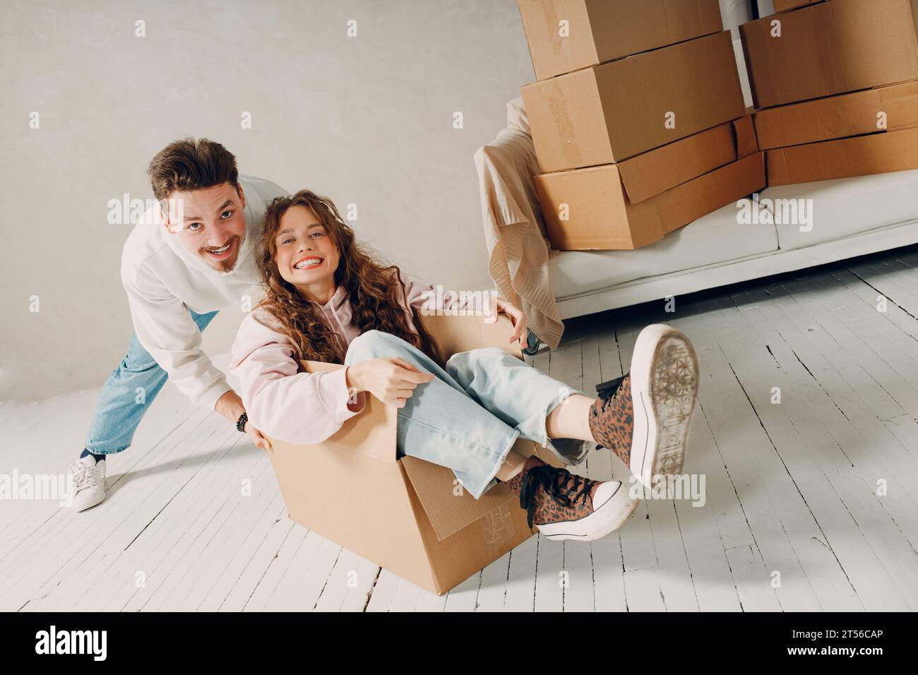 Happy young family couple man haul move woman inside box. Moving with ...