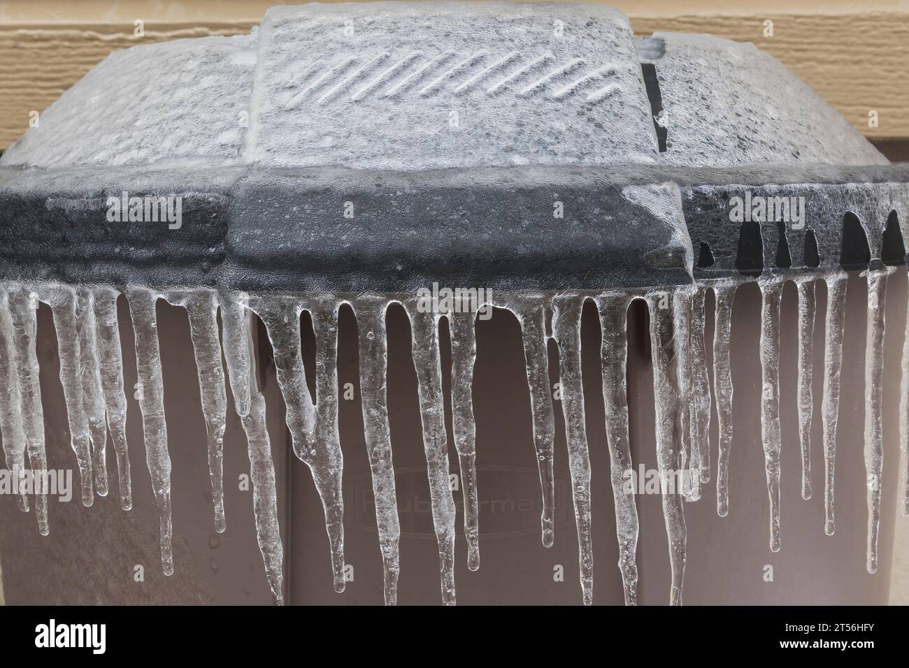 Brown and black plastic trash can covered with ice and icicles, Quebec ...