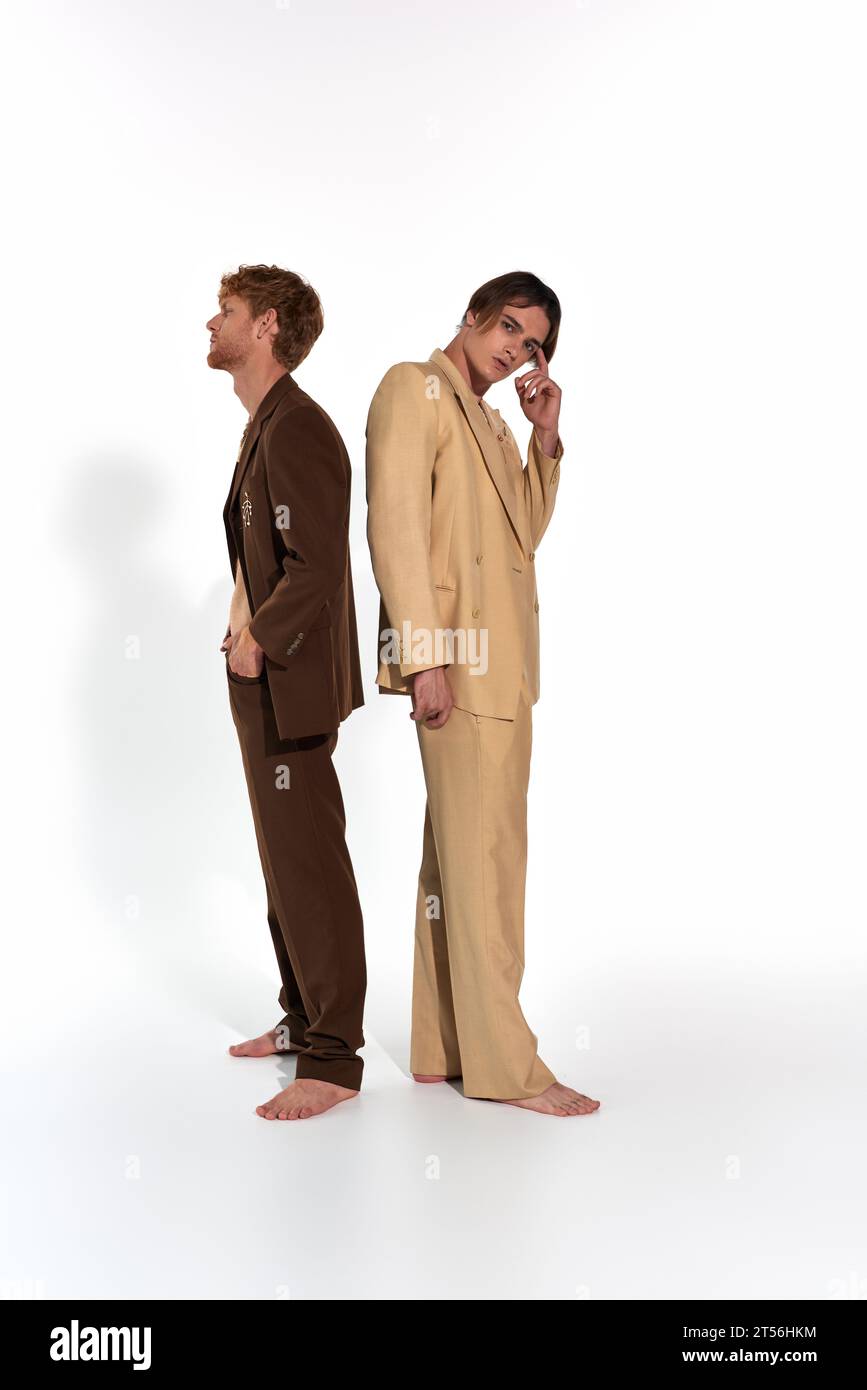 vertical shot of two appealing male models in suits posing back to back ...