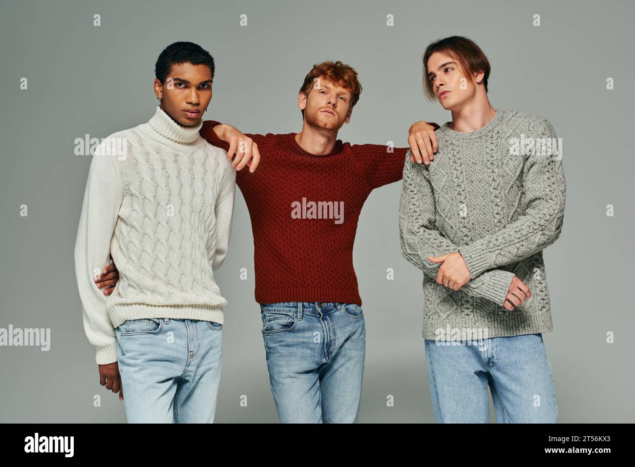 three handsome male friends in vibrant sweaters and jeans posing on ...