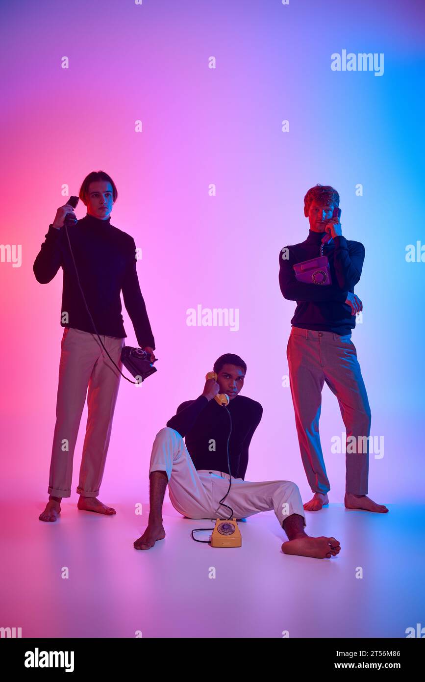 vertical shot of diverse trio in black attire surrounded by neon lights ...
