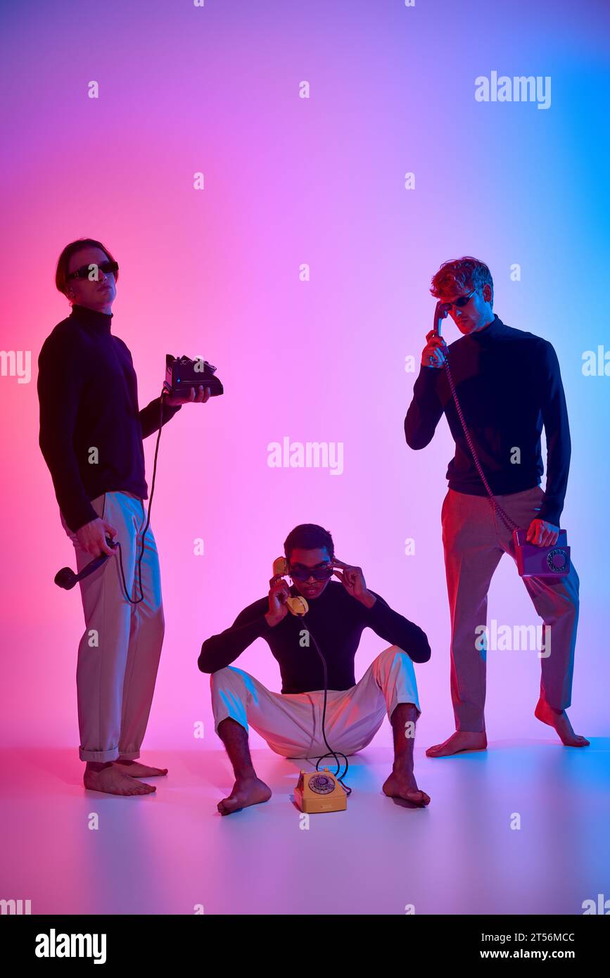 vertical shot of interracial trio encircled by neon lights talking on ...