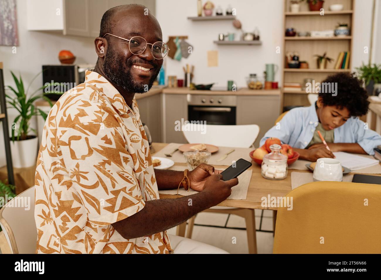 Smiling Black man answering text messages from colleagues when his son ...