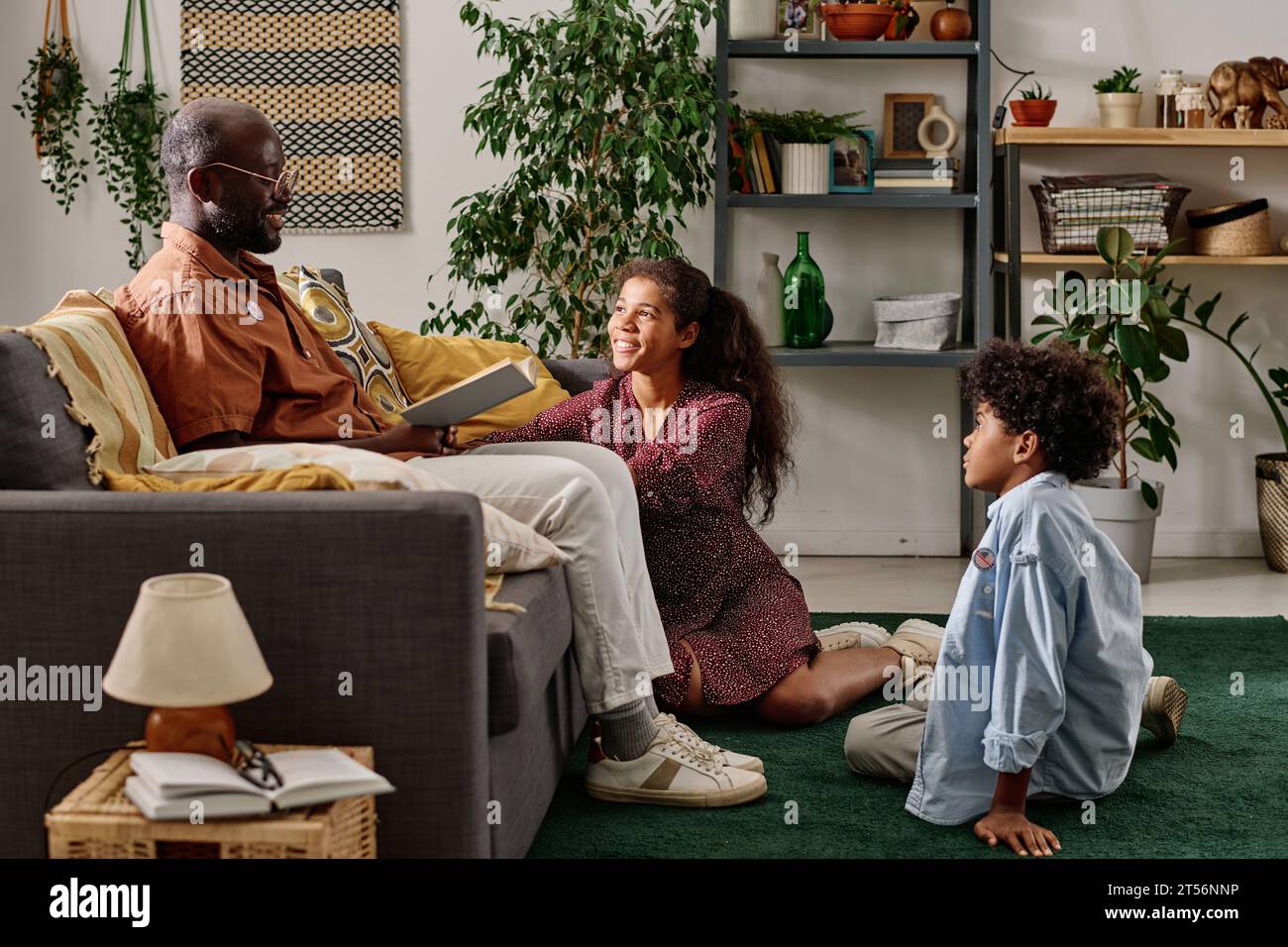 Cheerful son and daughter asking father to read book on African ...