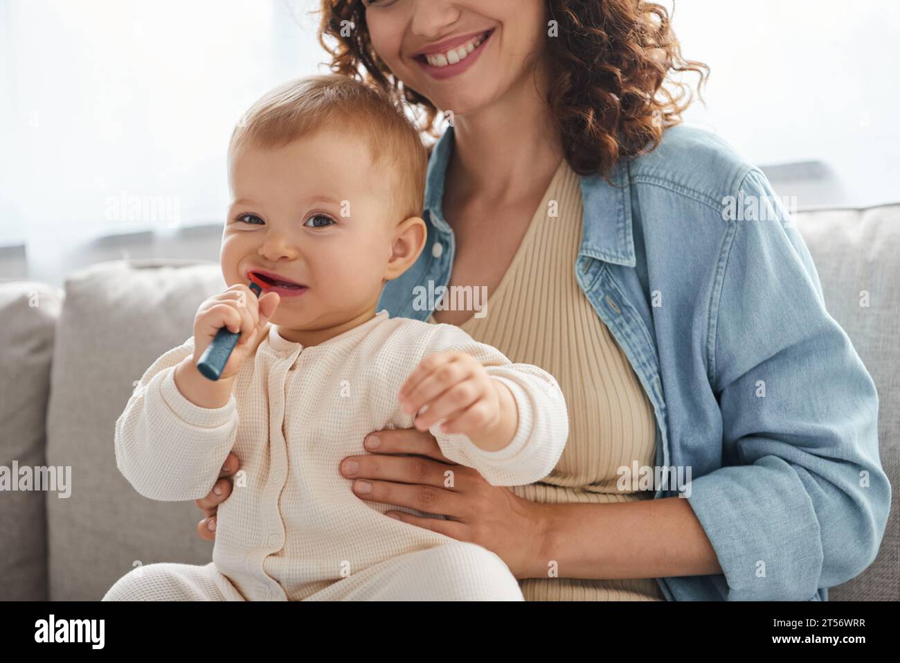 little girl chewing teething toy near smiling happy on couch in living ...
