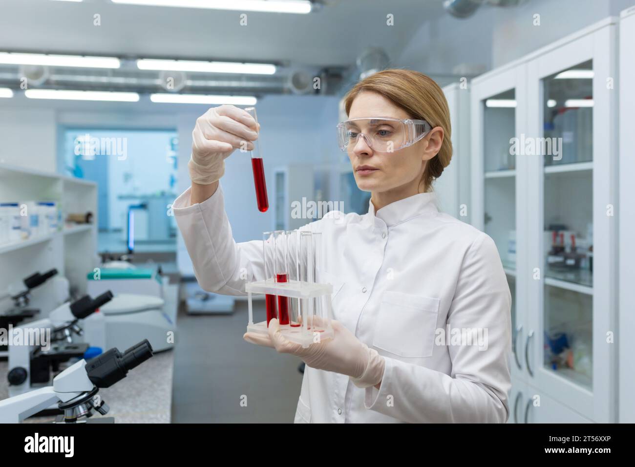 Concentrated and thinking woman in white medical coat examines blood ...