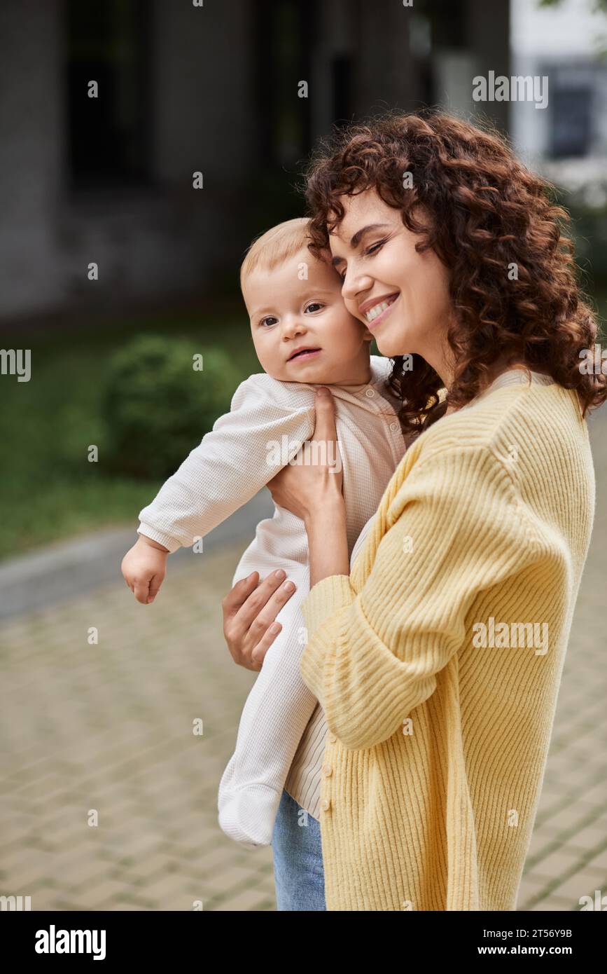 overjoyed woman with closed eyes holding and hugging adorable baby girl ...