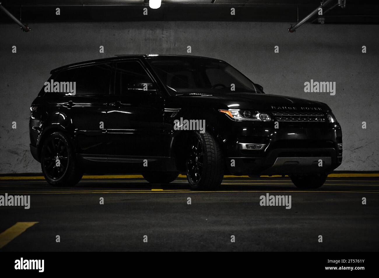 A black Range Rover is parked in a parking garage illuminated by light ...