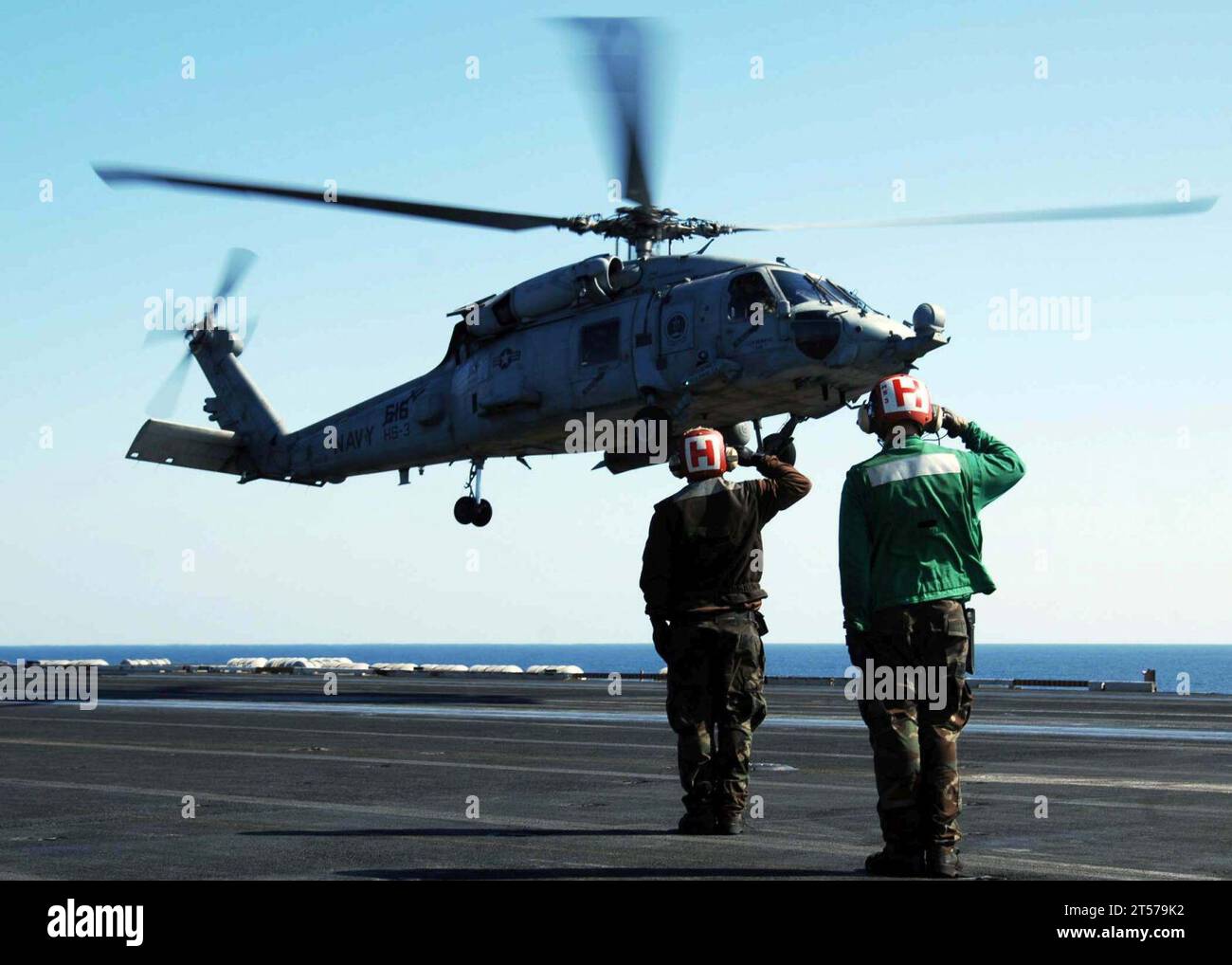 US Navy Sailors on the flight deck salute a pilot as an HH-60H Sea Hawk ...