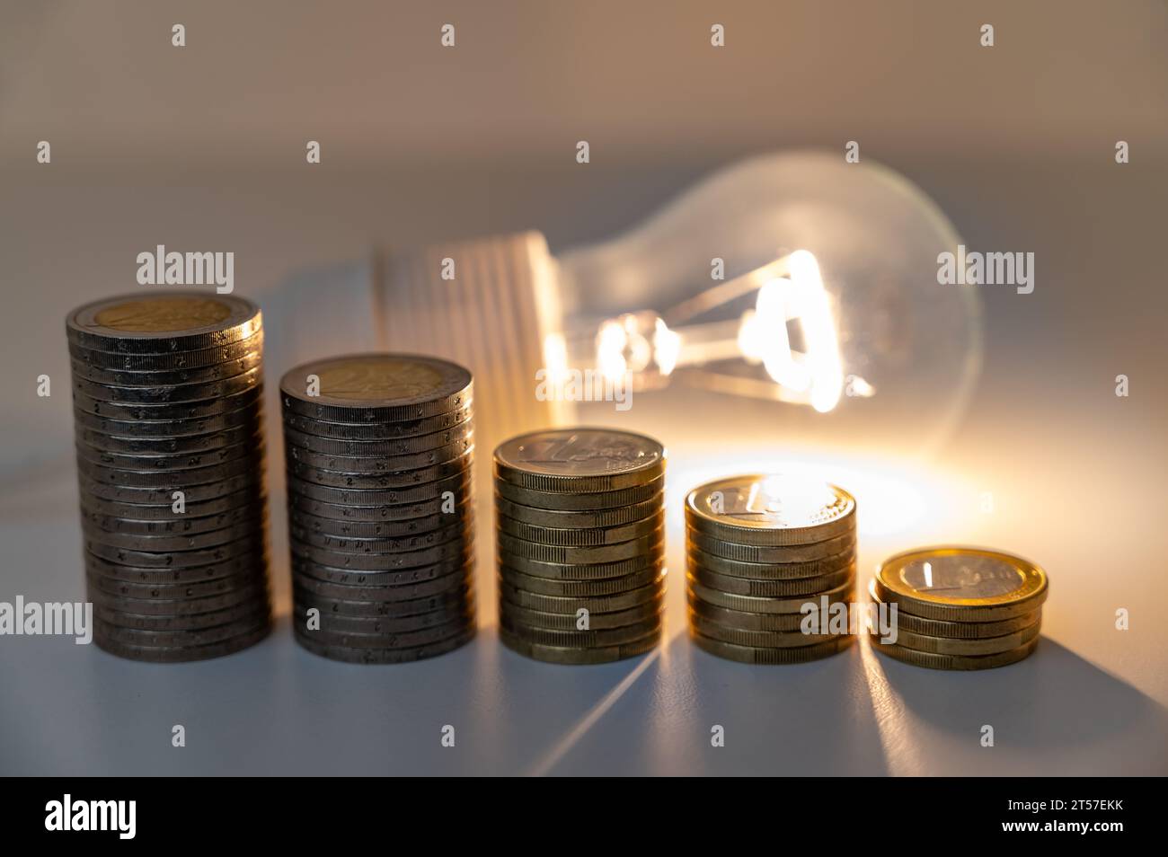 Light bulb lit with stacks of coins of descending height. Reduction in ...
