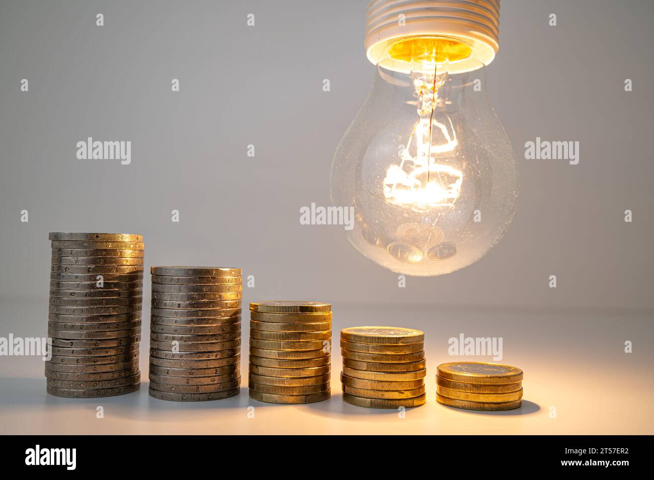 Light bulb lit with stacks of coins of descending height. Reduction in ...