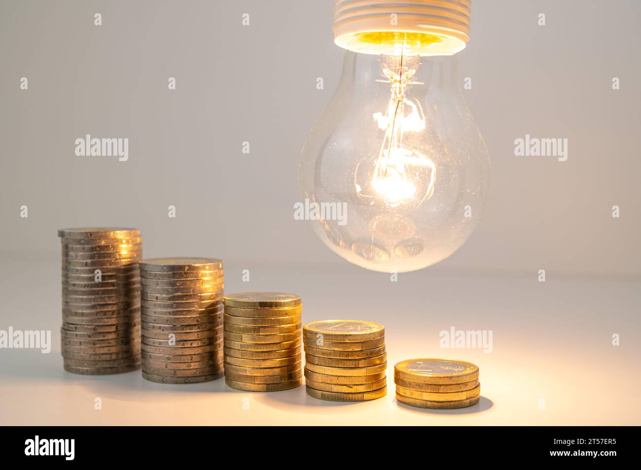 Light bulb lit with stacks of coins of descending height. Reduction in ...