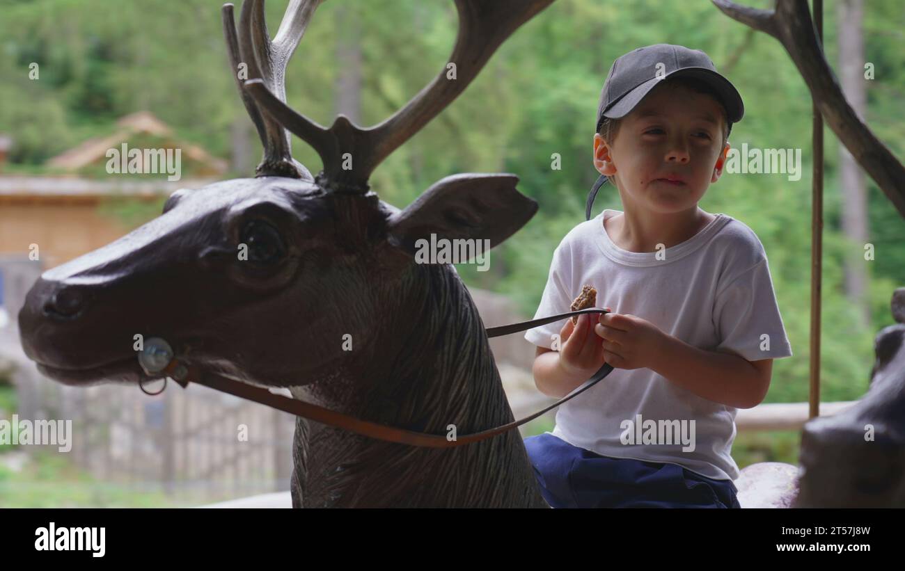 Happy child riding carousel on top of deer circus toy. Little boy ...