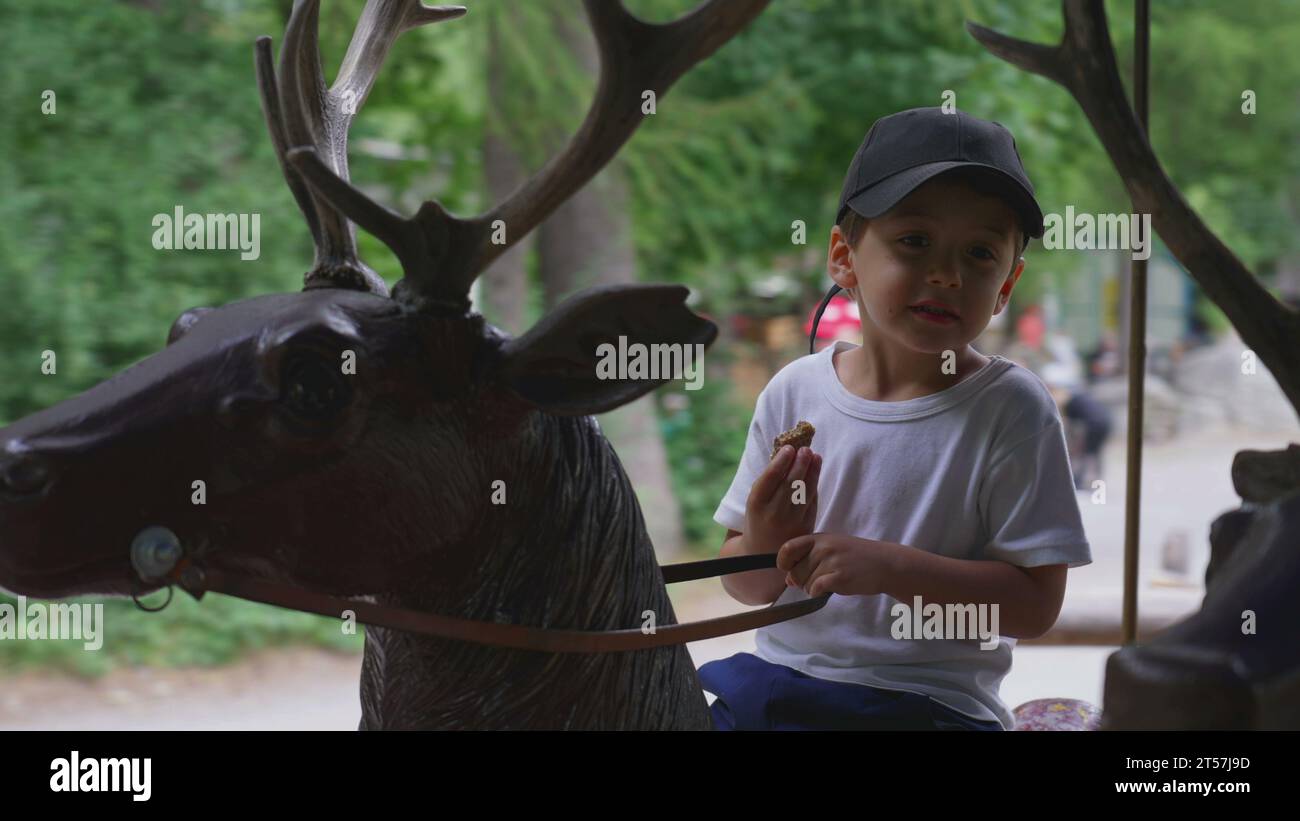 Happy child riding carousel on top of deer circus toy. Little boy ...