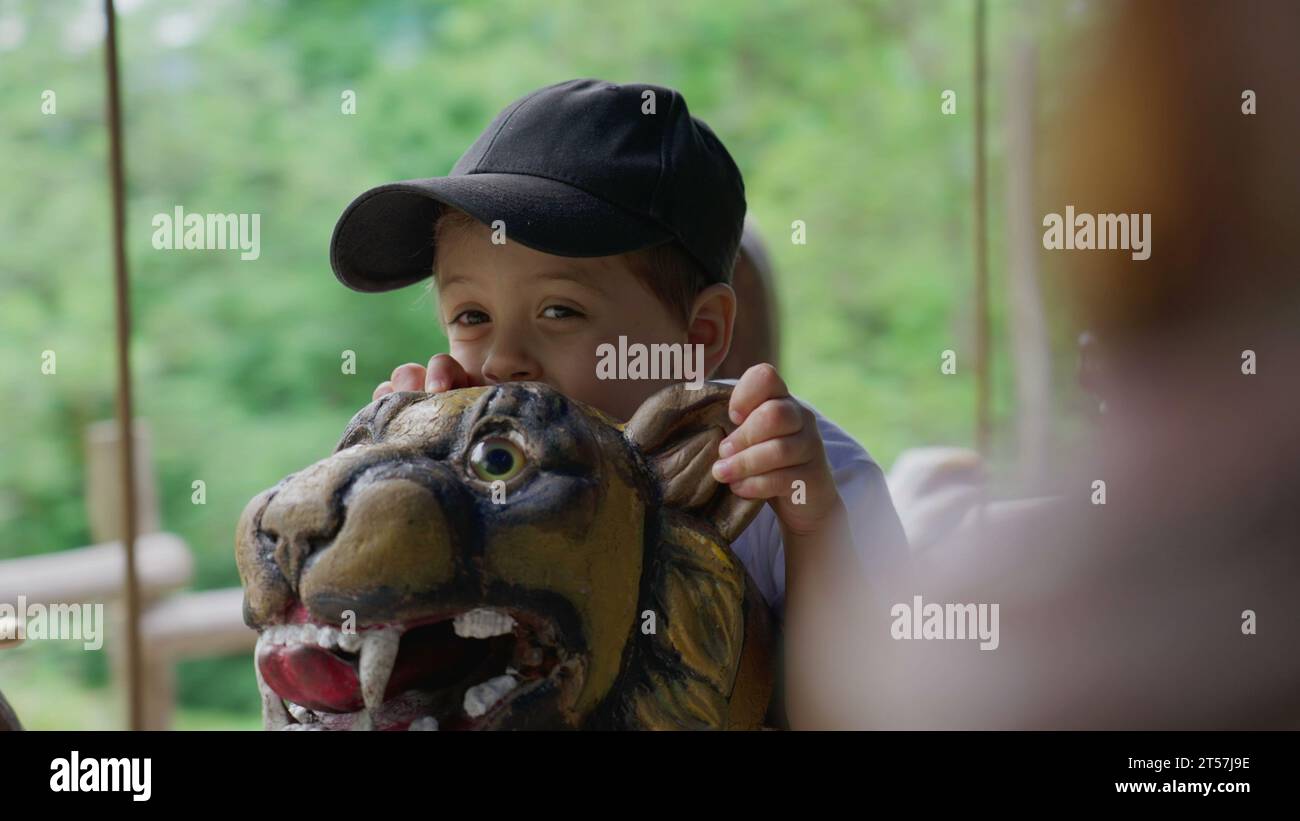 Happy small boy riding carousel at park, kid enjoying summer day seated ...