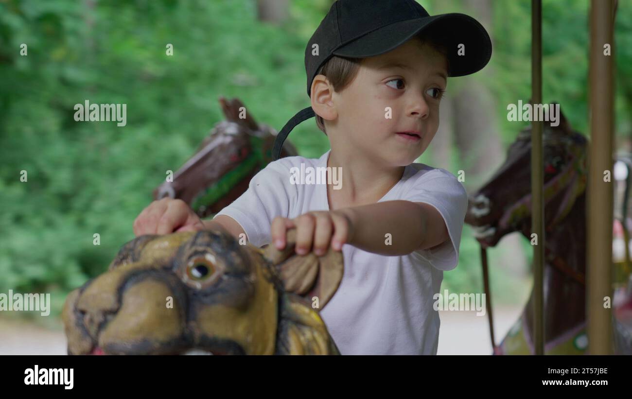 Happy small boy riding carousel at park, kid enjoying summer day seated ...