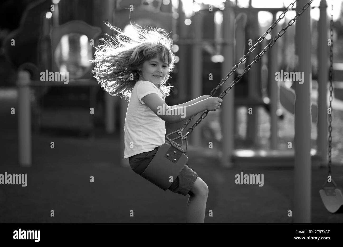 Child swinging on the playground. Child playing on the playground in kindergarten. Joyful kid on ...