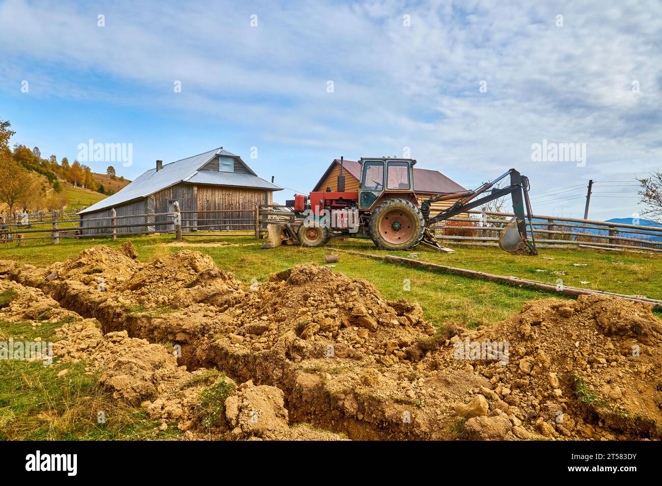 In the rural setting, a tractor is diligently excavating a trench for ...