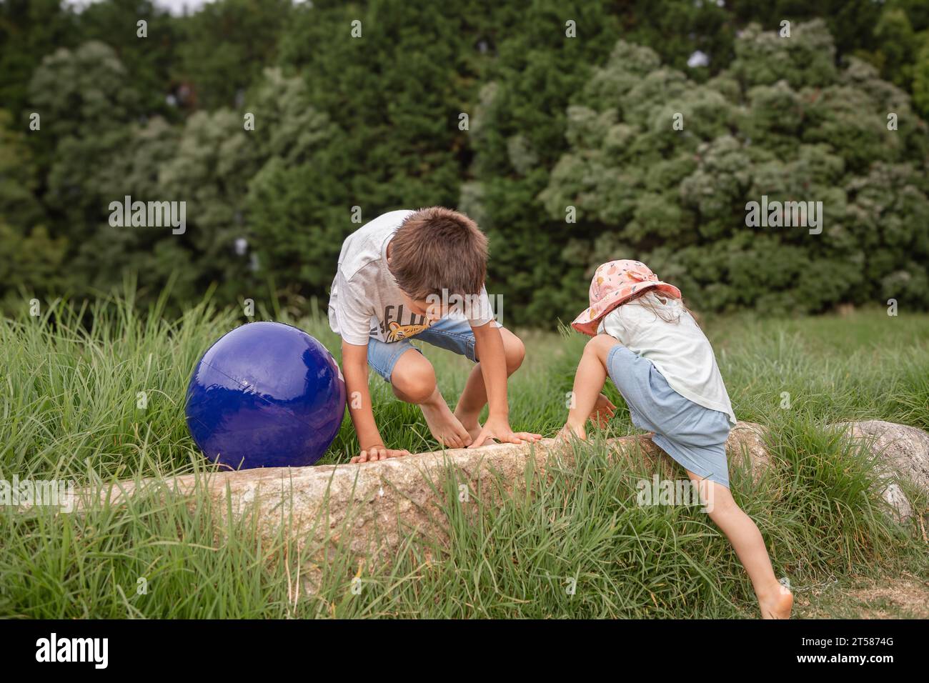 Two barefoot caucasian children playing up and down rocks in a green ...