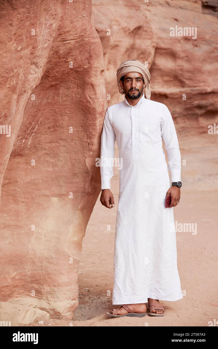 Portrait of Bedouin in white Thobe leaning against red rock, Wadi Rum ...