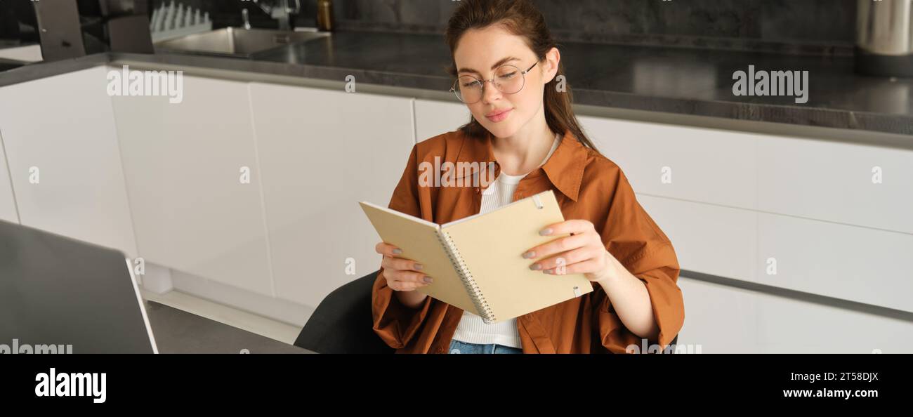 Close up portrait of young woman, student in kitchen, holding notebook ...