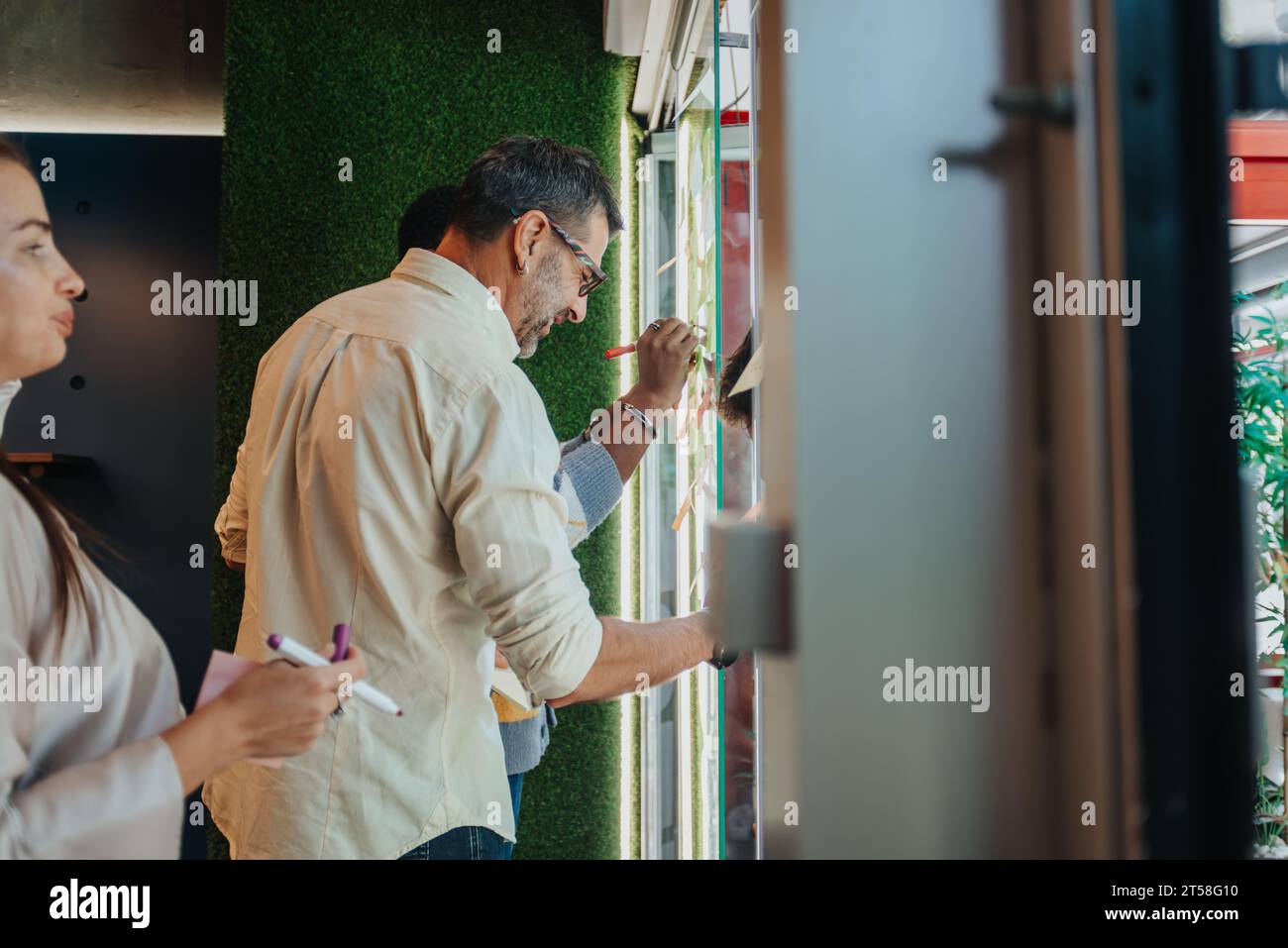 Diverse team collaborates, brainstorming ideas, writing on sticky notes ...