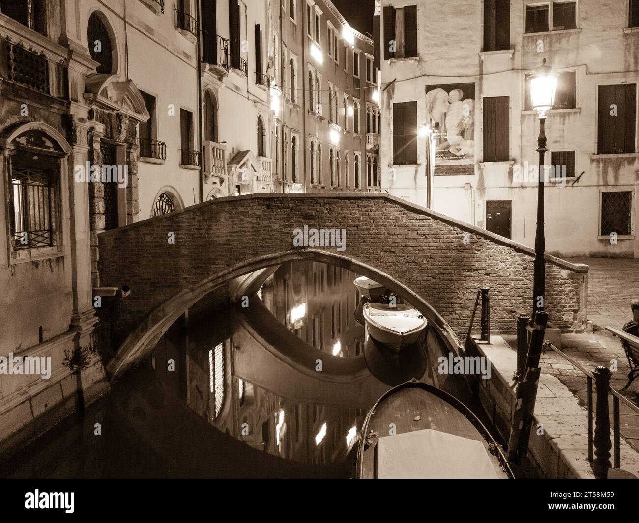 A bridge in Venice, Italy, at night. Boats are moored on the quays ...