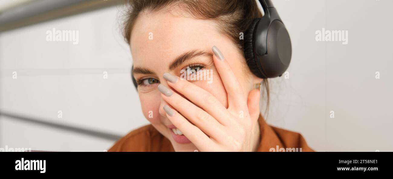 Cute smiling girl, blushes, hides face behind hand and laughing, wears ...