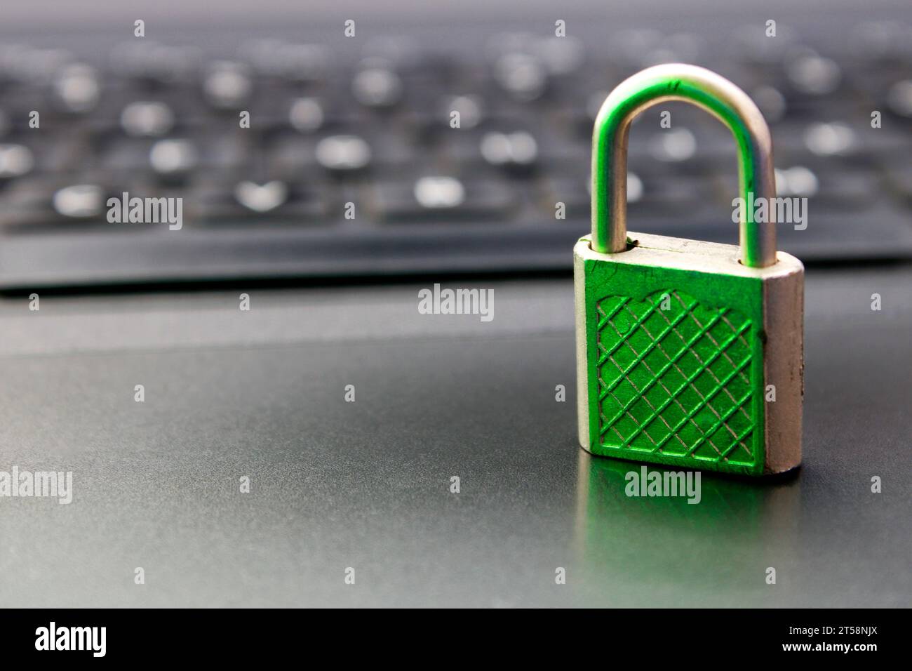 Closed padlock with green light reflection indicating security on computer keyboard background ...