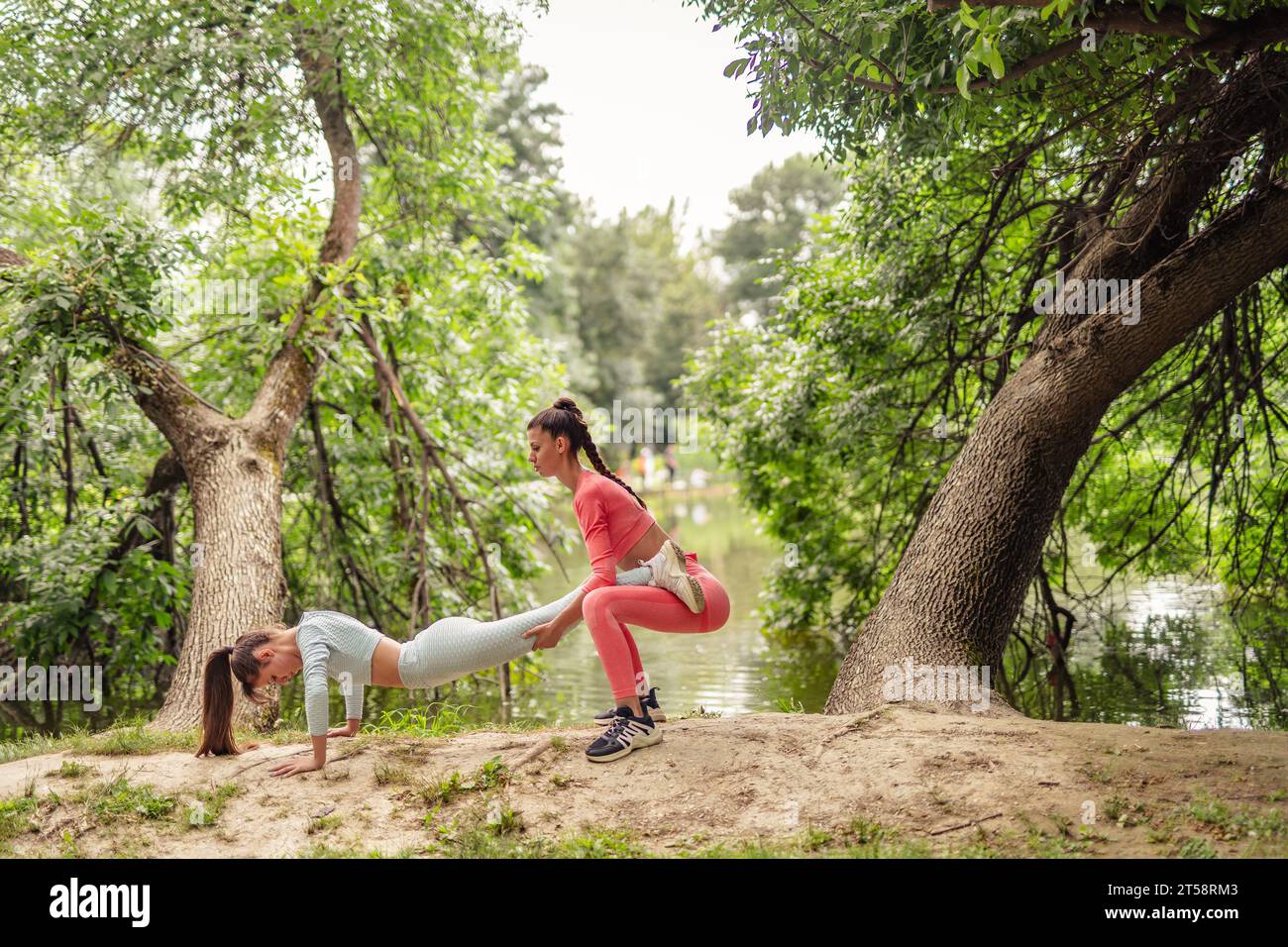 Two fit females exercising outdoors in an urban park, stretching and ...