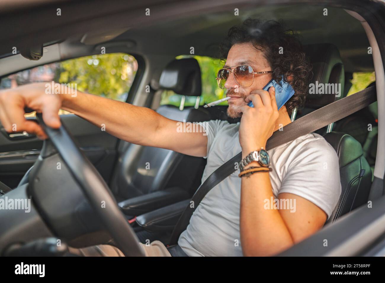 Man with curly hair driving a car, smoking a cigarette and using phone ...