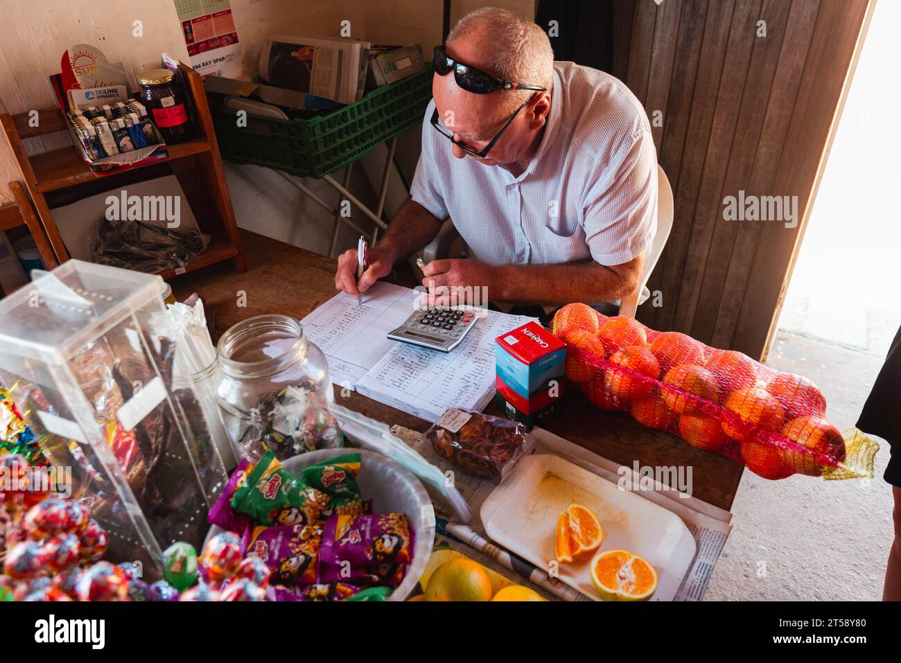 A shop owner does his daily accounts with a pen, calculator and book at ...