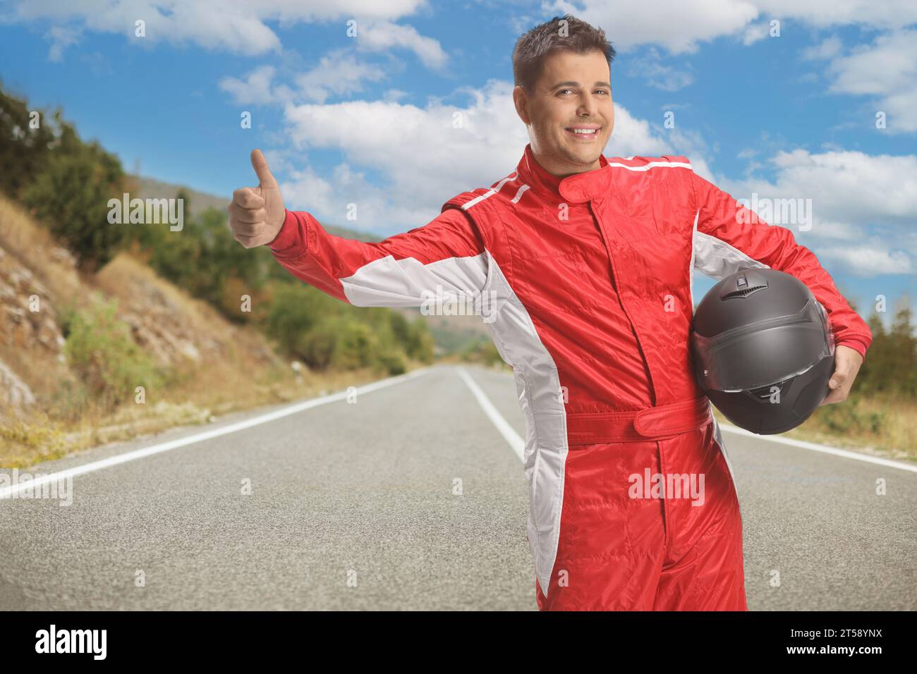 Racer in a red suit holding a helmet and hitchhiking on an open road ...