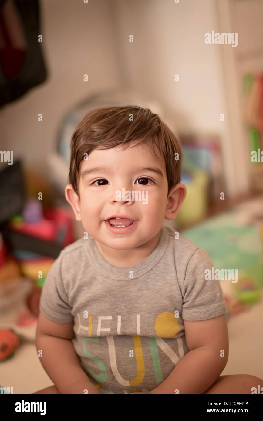 Cute little boy looking at camera while sitting on the floor at home ...