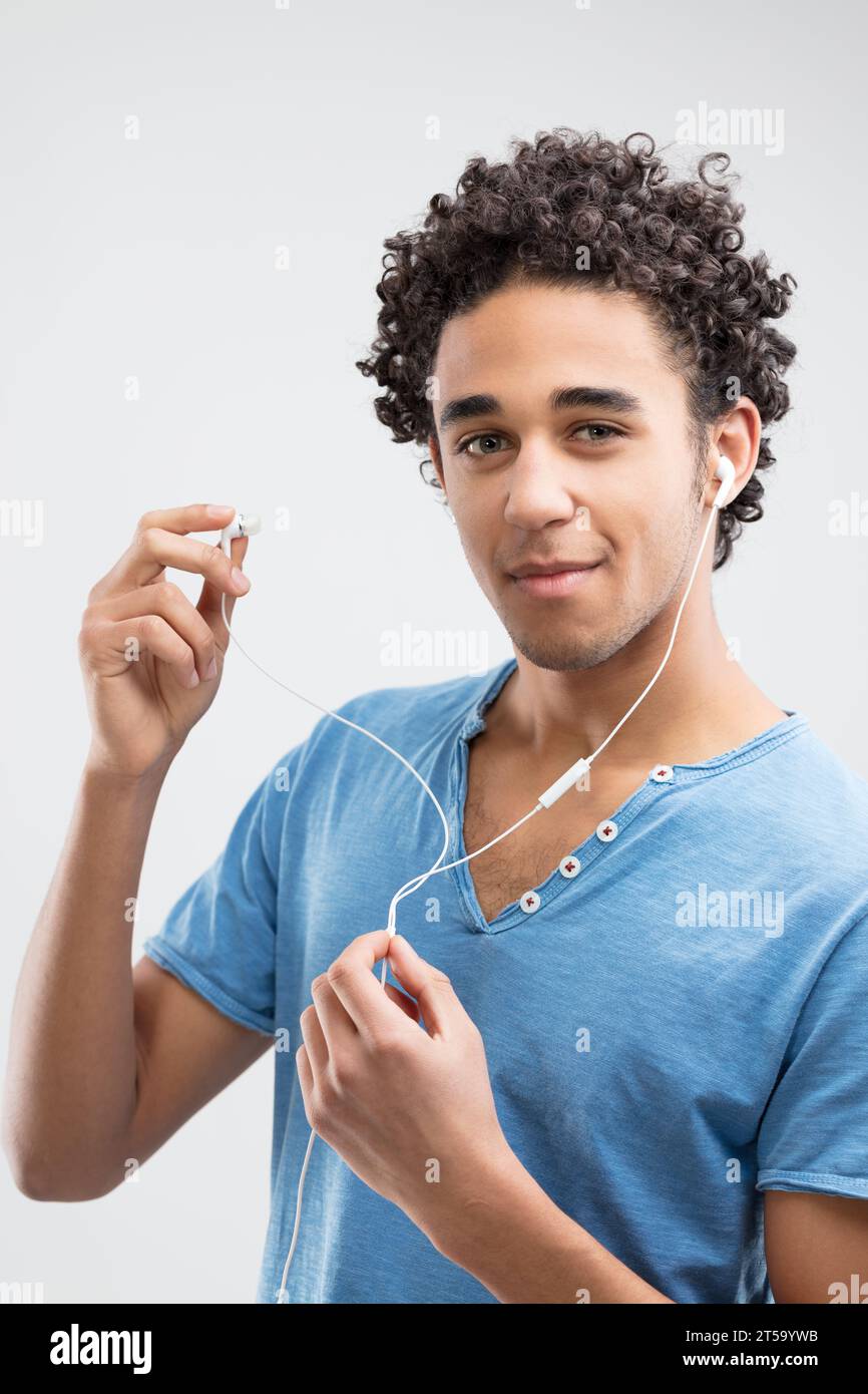 Young smiling man with curly hair showcases white earbuds, wearing a blue shirt Stock Photo - Alamy