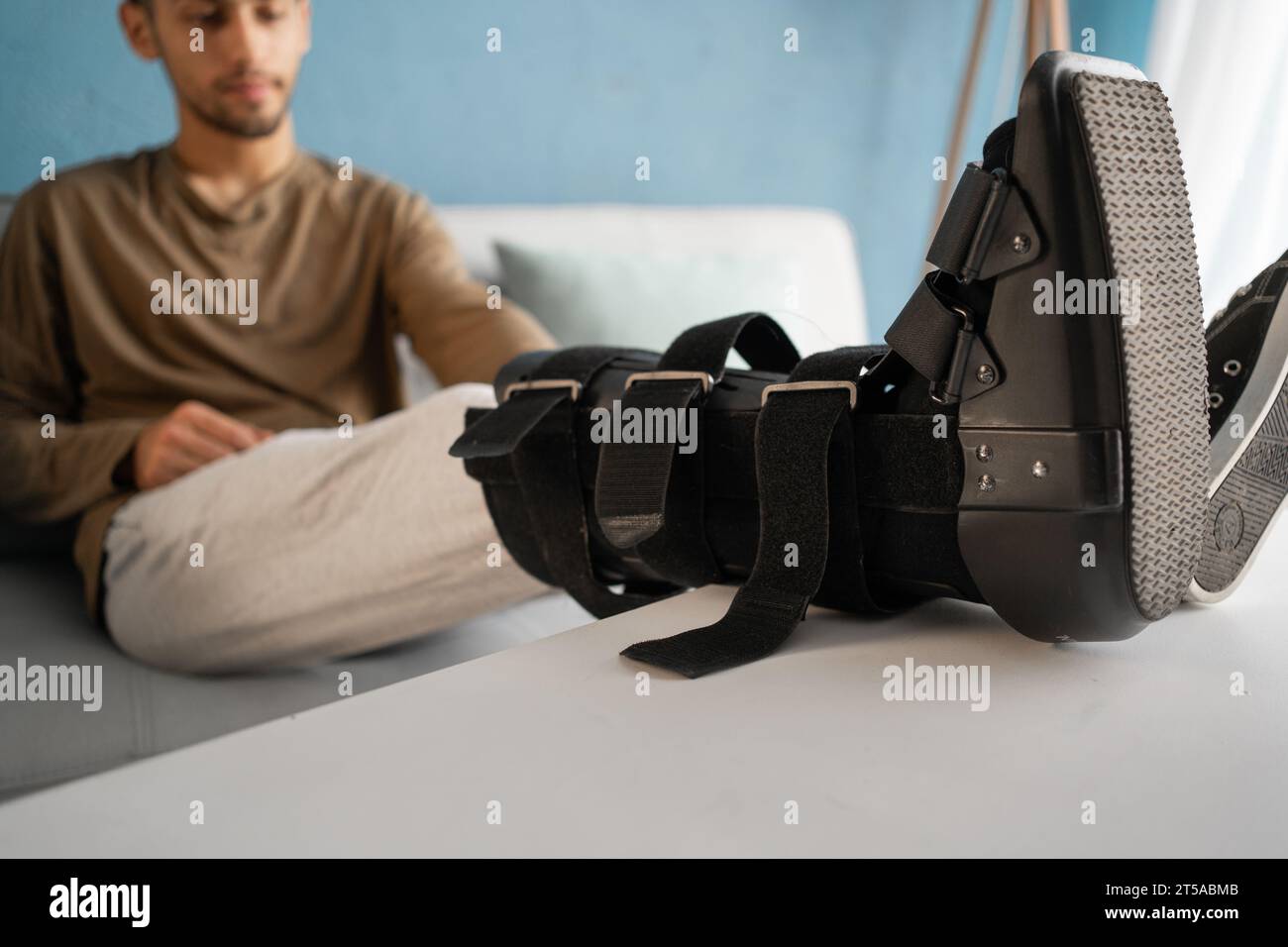 Young man with ankle orthosis, walker boot on leg sitting on the sofa at home, close-up Stock ...